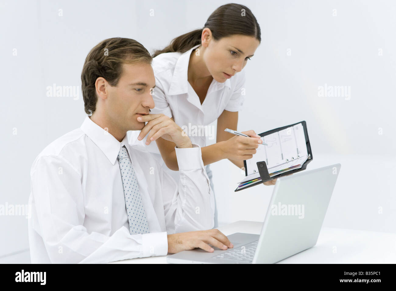 Professional man using laptop, assistant looking over his shoulder and ...