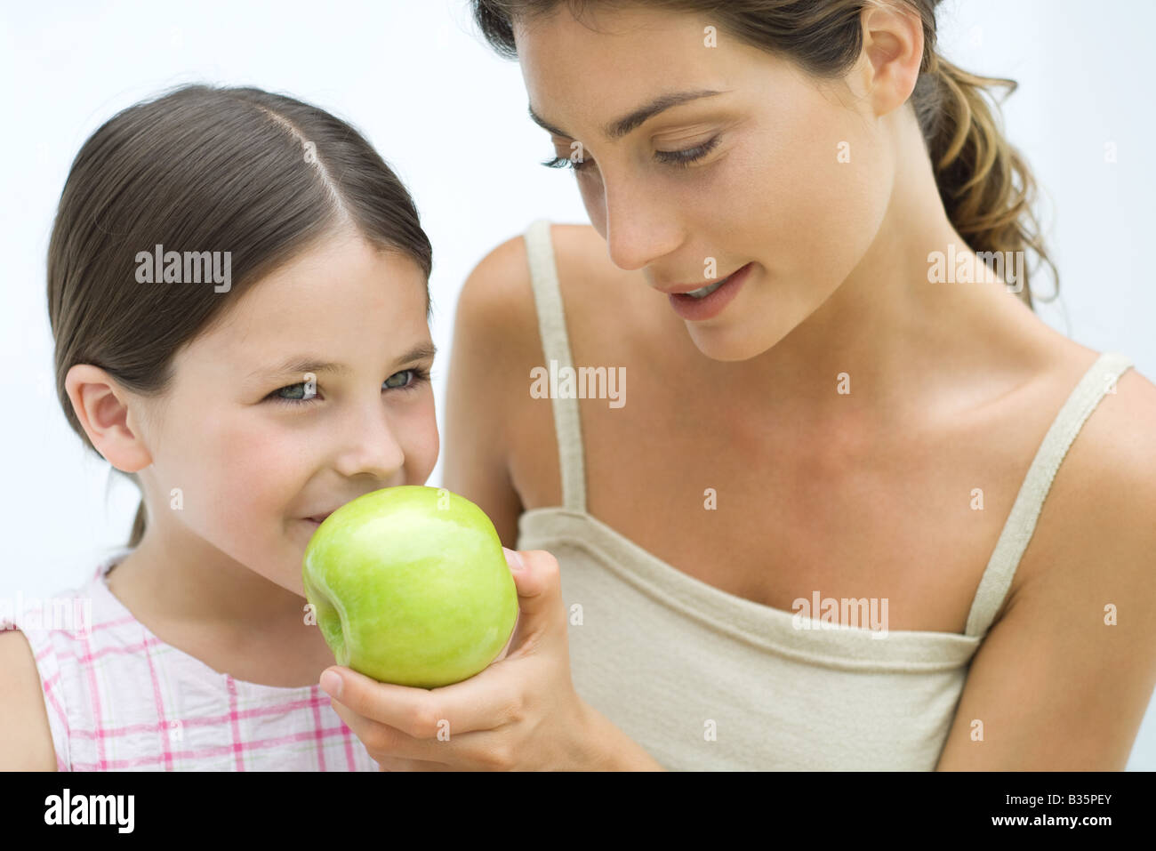 Mother giving daughter an apple, both smiling Stock Photo - Alamy