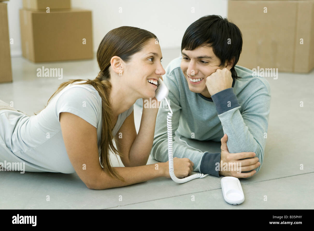Couple lying on the floor, woman talking on landline phone, boxes in ...
