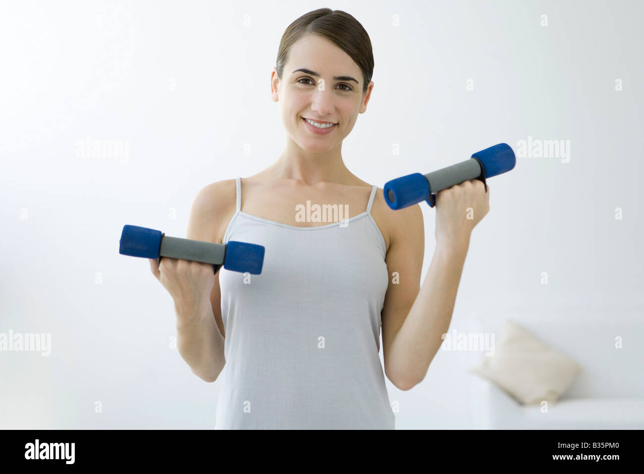 Young woman lifting dumbbells, smiling at camera Stock Photo - Alamy