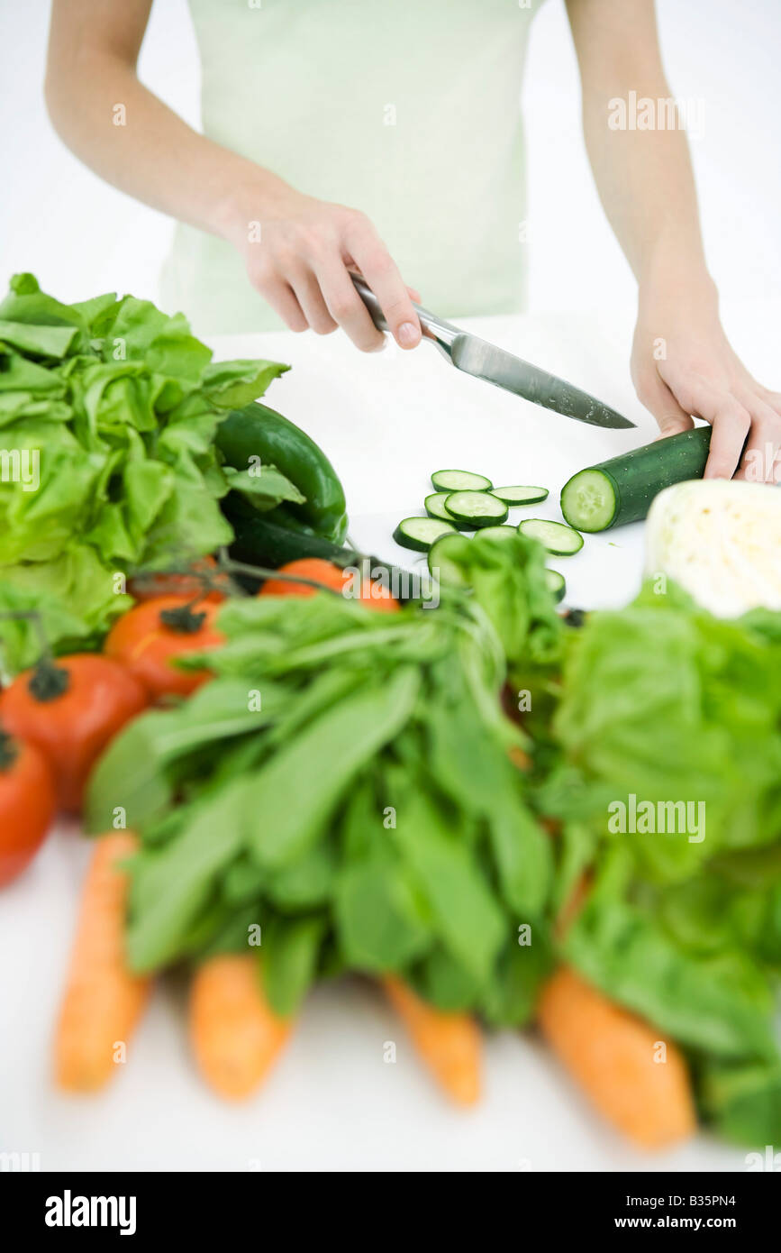 Woman slicing cucumber, assorted vegetables in foreground, cropped view ...