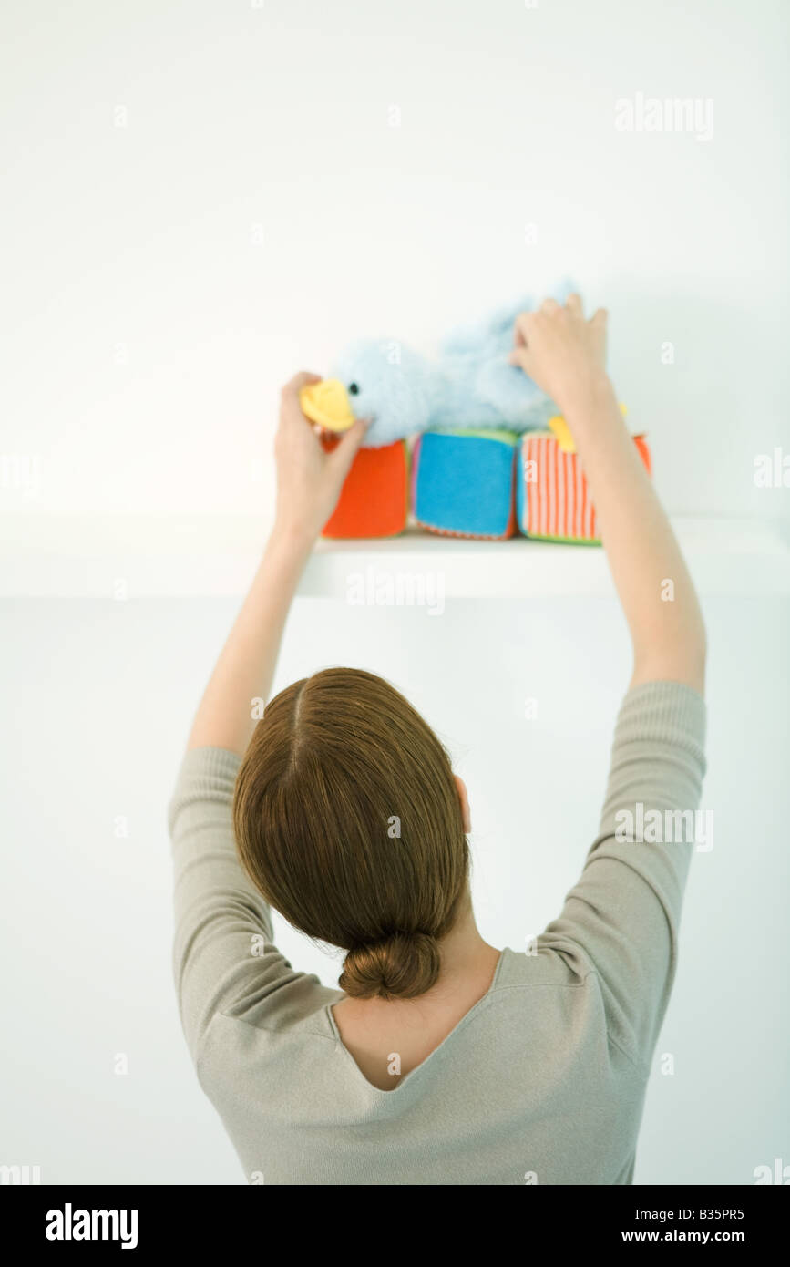 Woman placing stuffed toy on shelf, rear view Stock Photo - Alamy