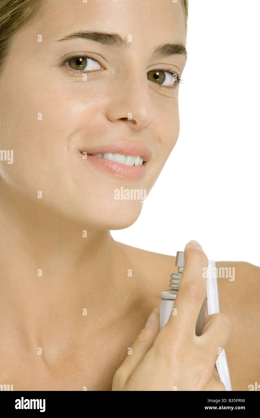 Woman spraying perfume on her neck, smiling at camera Stock Photo - Alamy