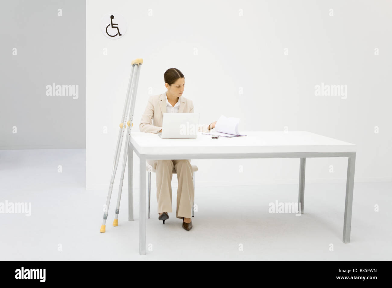 Professional woman working in office, crutches leaning against desk ...