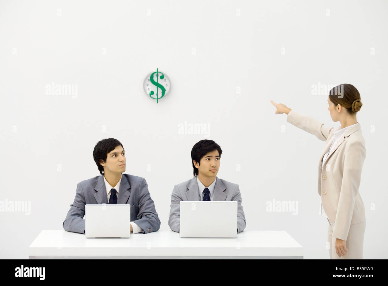 Two male office workers sitting at desk, female supervisor pointing at ...