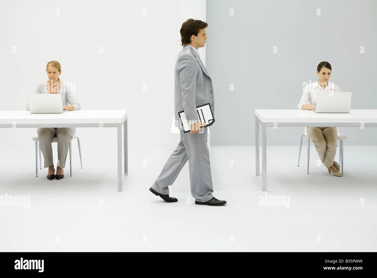 Businessman walking in office, carrying document under arm, female ...