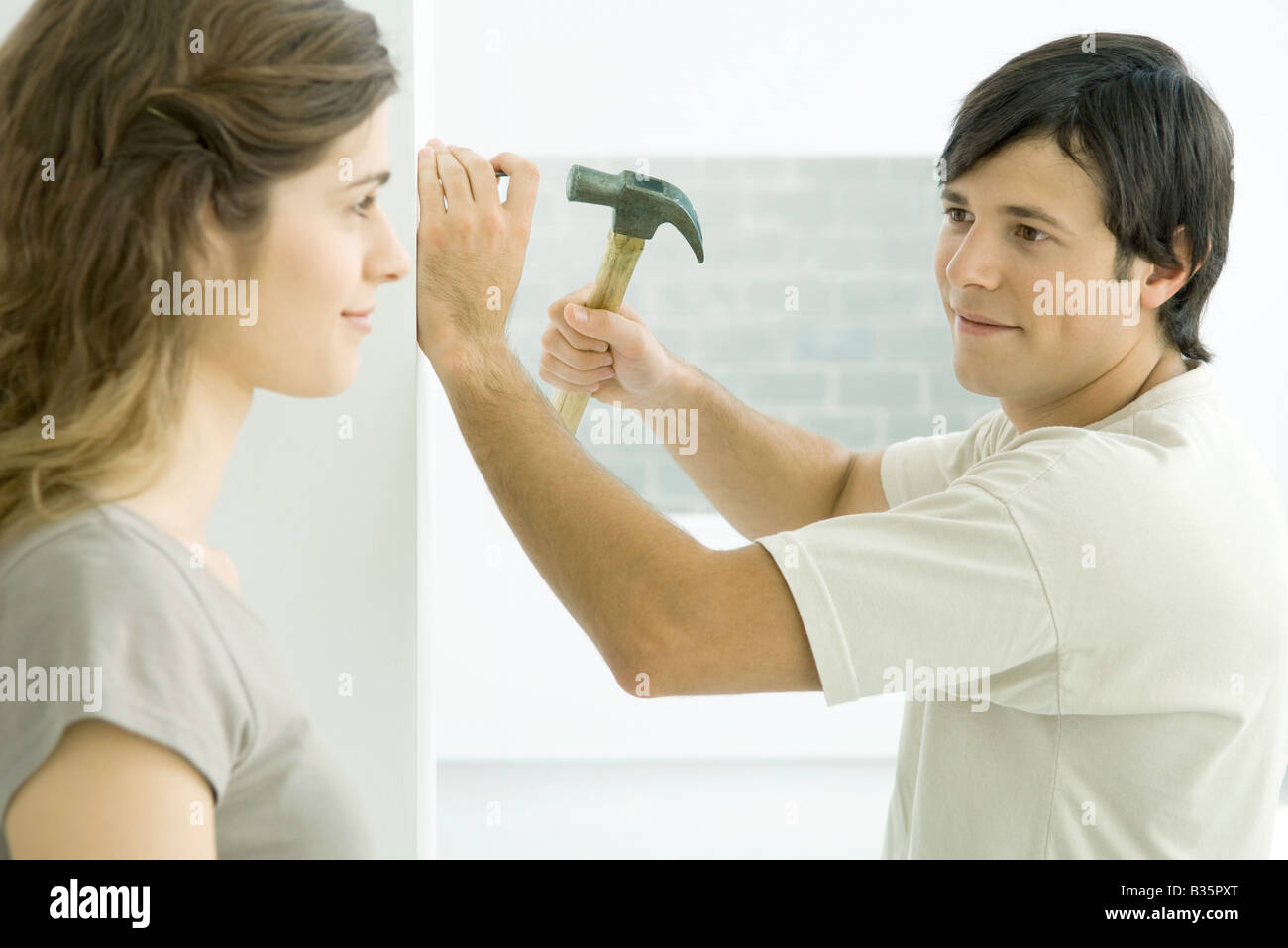 Couple smiling at each other, man hammering nail into wall Stock Photo ...
