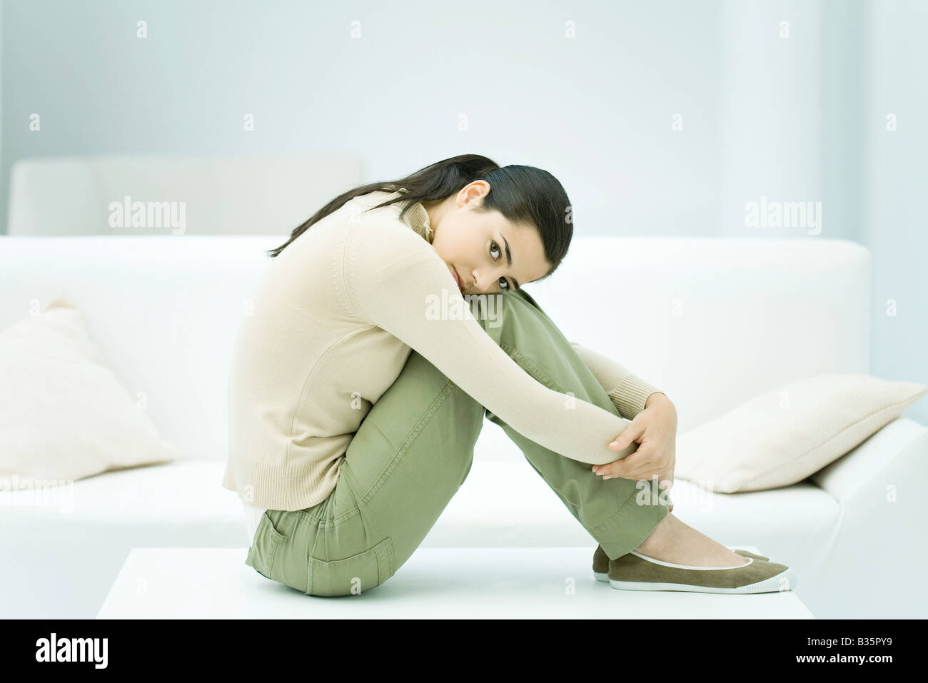 Woman sitting on coffee table, hugging knees, looking at camera Stock ...