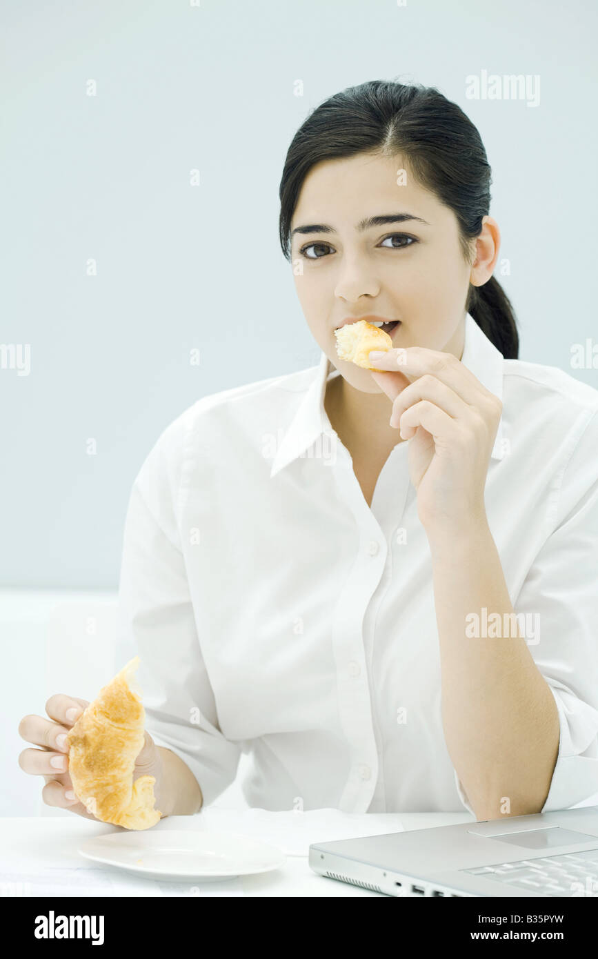 Young woman eating croissant, sitting at desk, looking at camera Stock ...