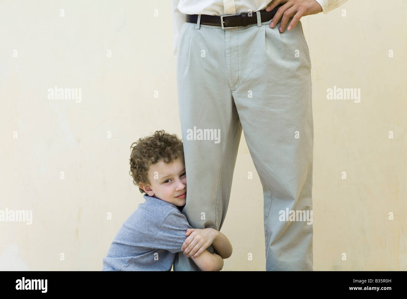 Boy clinging to his father's leg, looking at camera, cropped view Stock ...
