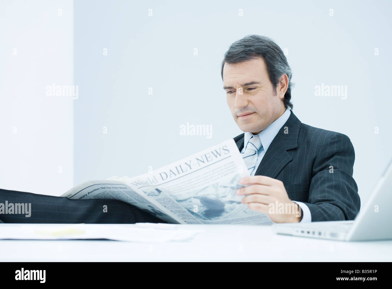 Businessman sitting at desk, reading newspaper, looking down with ...