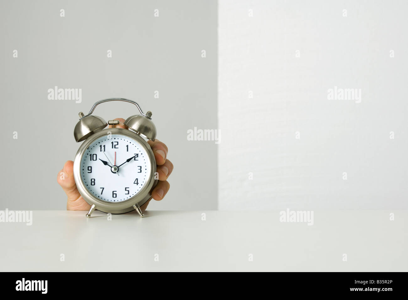 Old-fashioned alarm clock, hand reaching up to grab it from behind ...