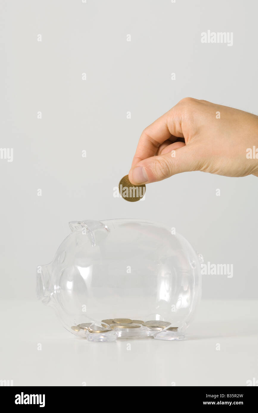 Hand dropping coin into transparent piggy bank Stock Photo - Alamy