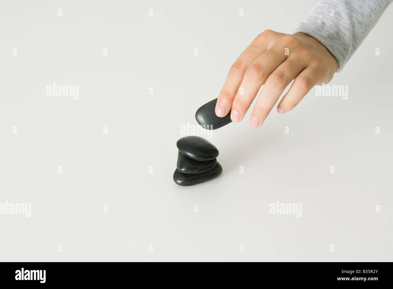 Hand stacking smooth black stones, cropped view Stock Photo - Alamy
