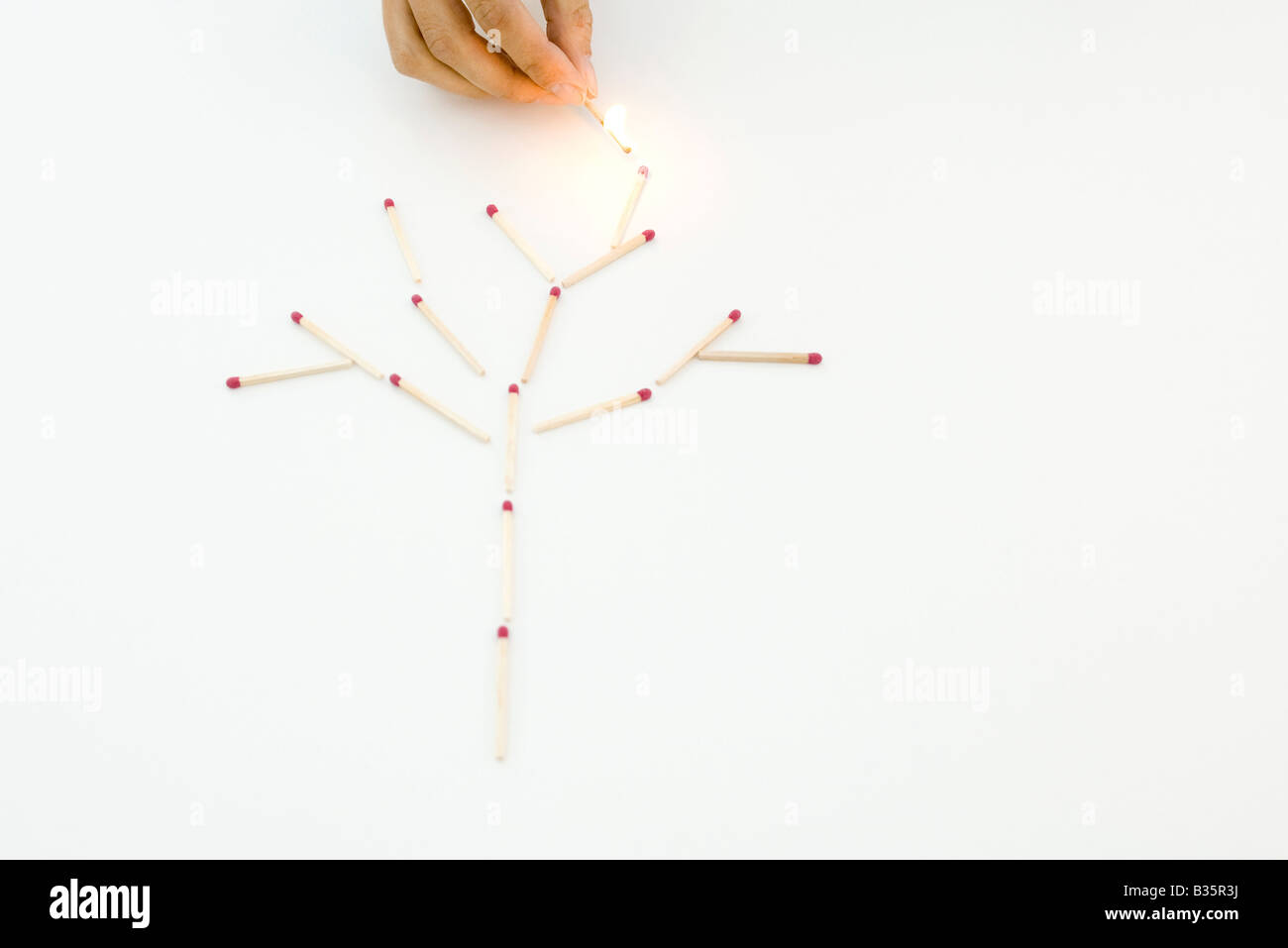 Hand holding a lit match, igniting matches arranged in a tree pattern ...