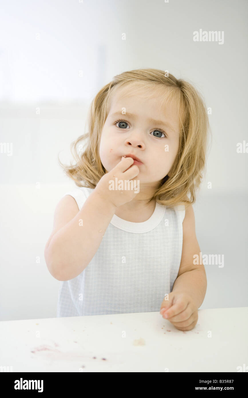 Little girl sitting at messy table, wiping a crumb off her lip Stock ...