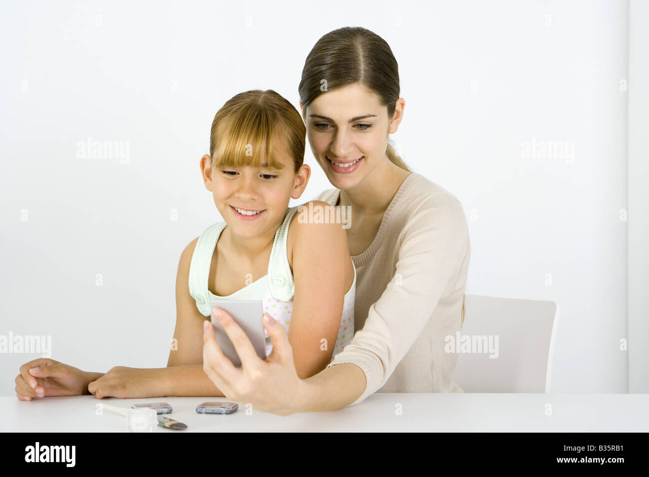 Girl sitting on young woman's lap, looking into hand mirror together ...