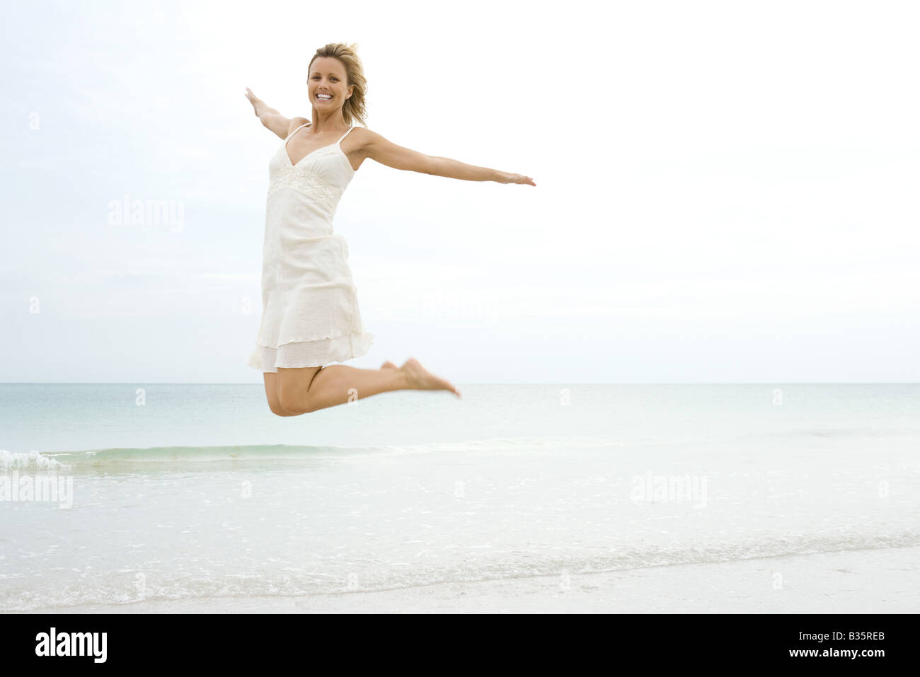 Woman leaping in midair at the water's edge, arms out and legs back ...