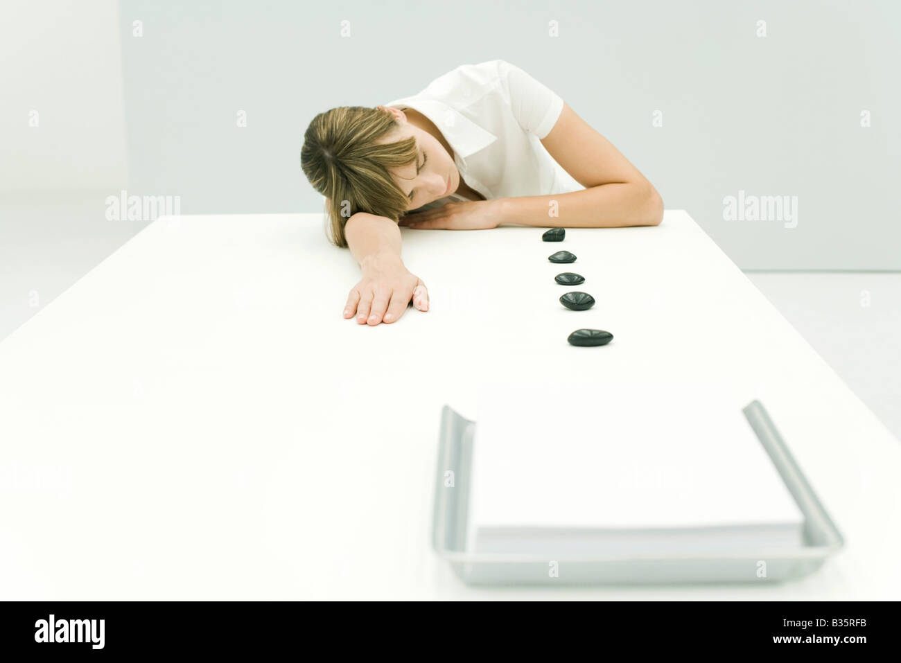 Woman resting head on table, lined up stones leading to stack of paper ...