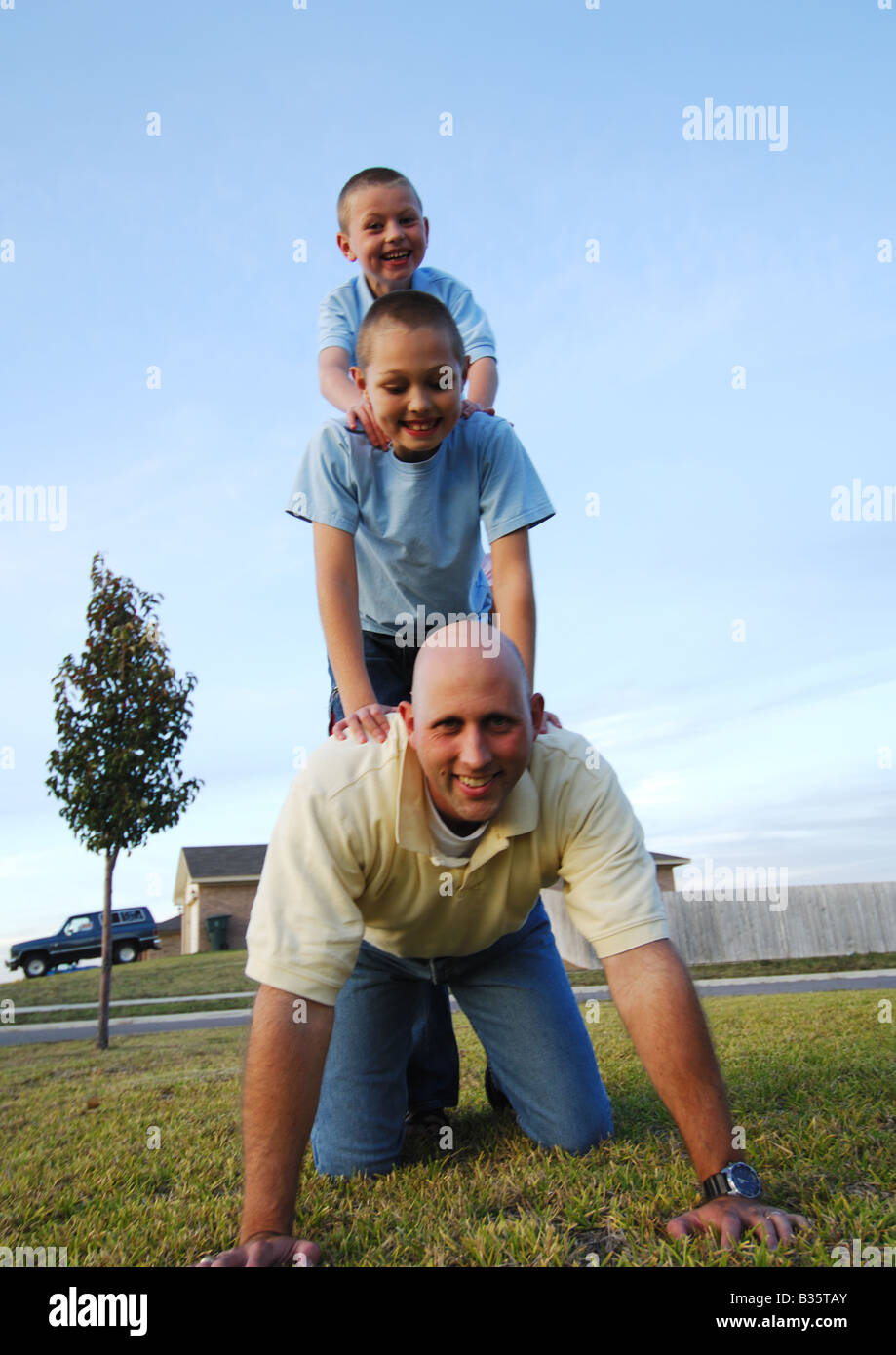 Two boys riding on their father's back Stock Photo - Alamy