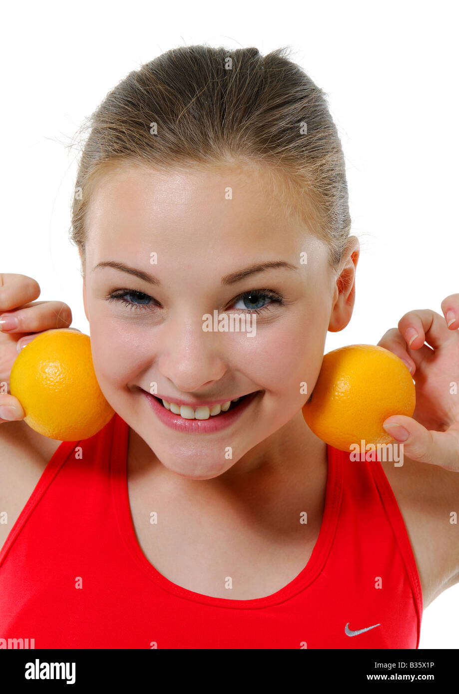Portrait of a young woman holding two oranges besides her two cheek and ...