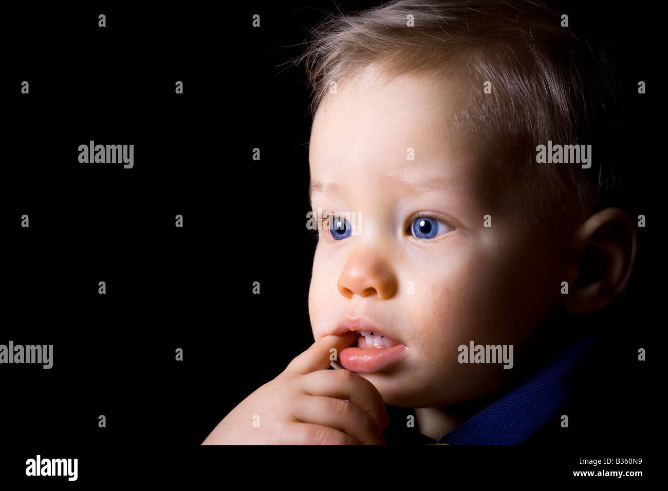 Close up of handsome blond boy with teething pain on black background ...