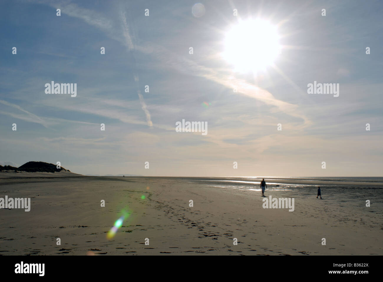 Silhouetted figures stroll along Talacre Beach in North Wales at sunset ...