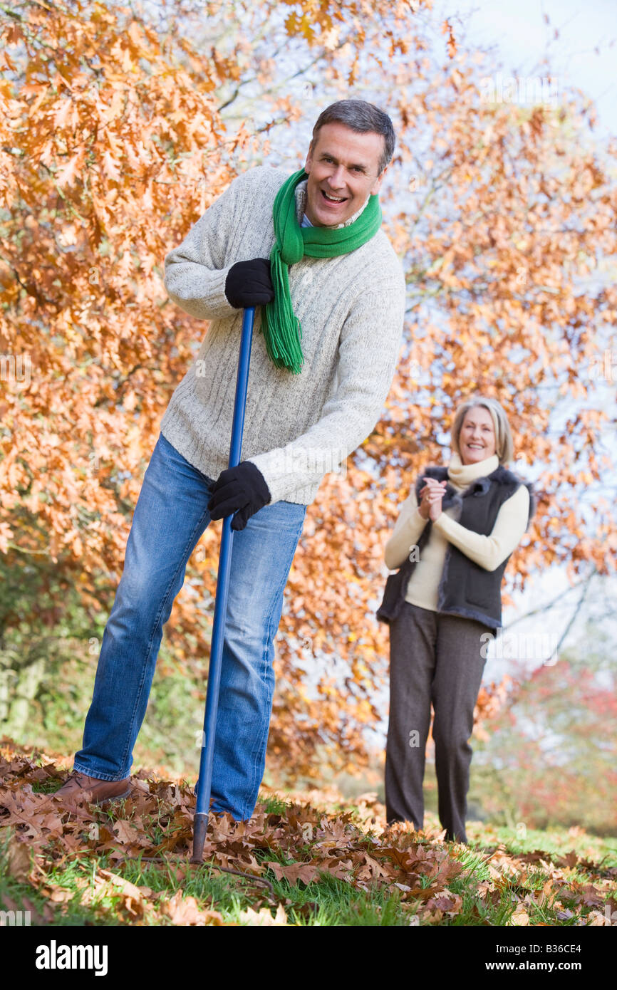 Man outdoors raking leaves and woman in background smiling (selective ...