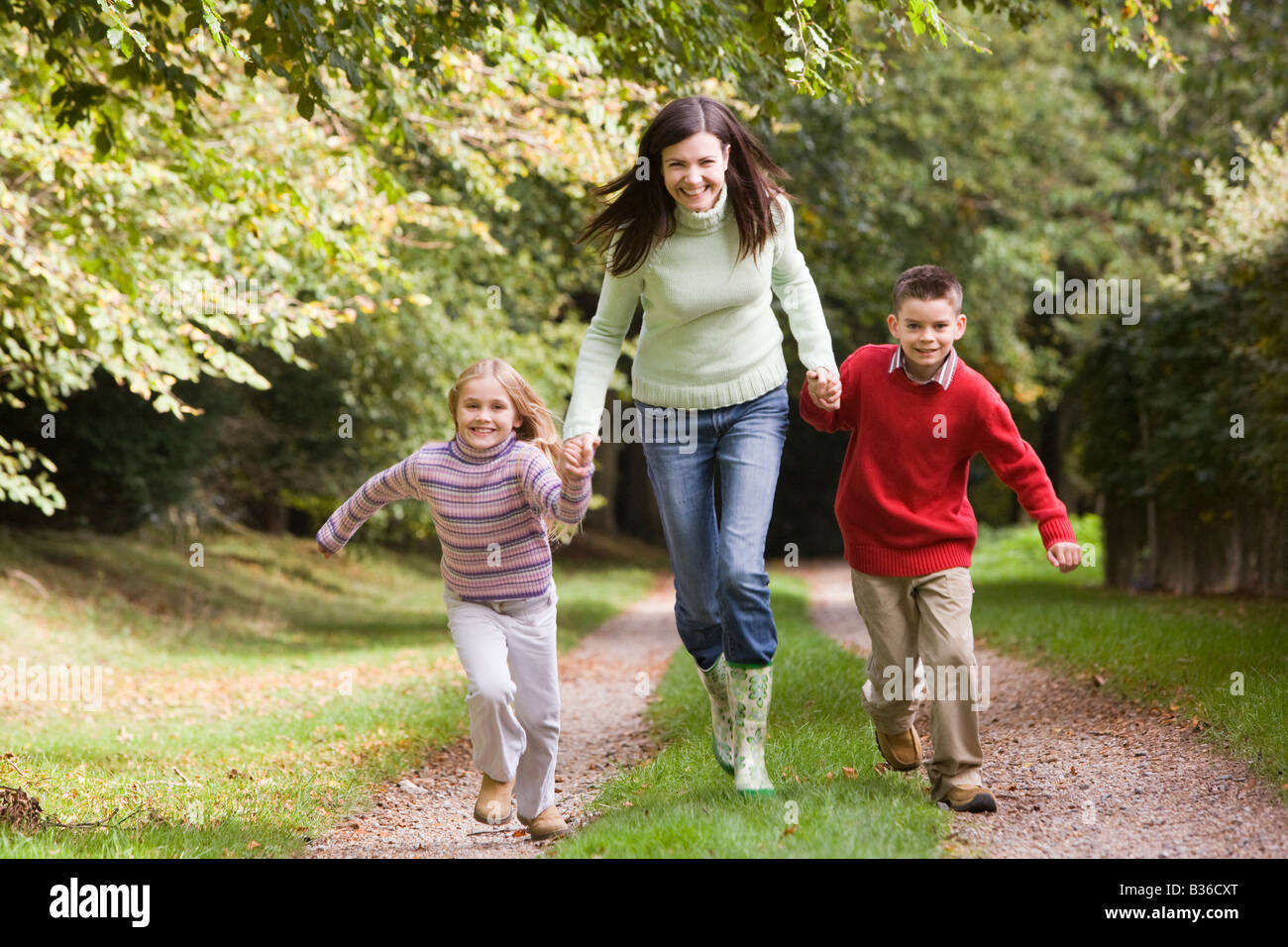 Woman outdoors with two young children walking on path holding hands and smiling (selective ...