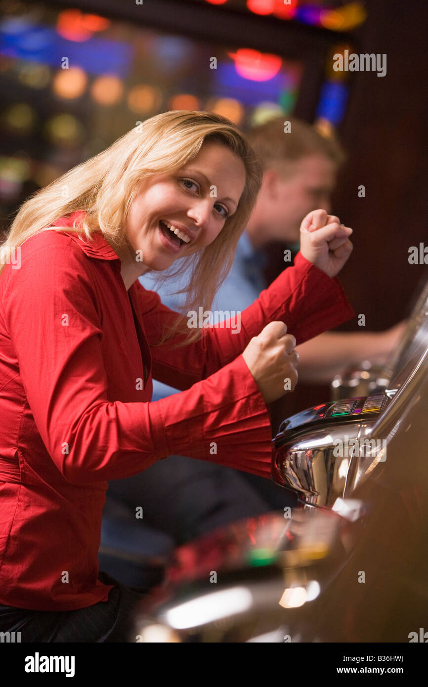 Woman in casino excited playing slot machine with people in background ...