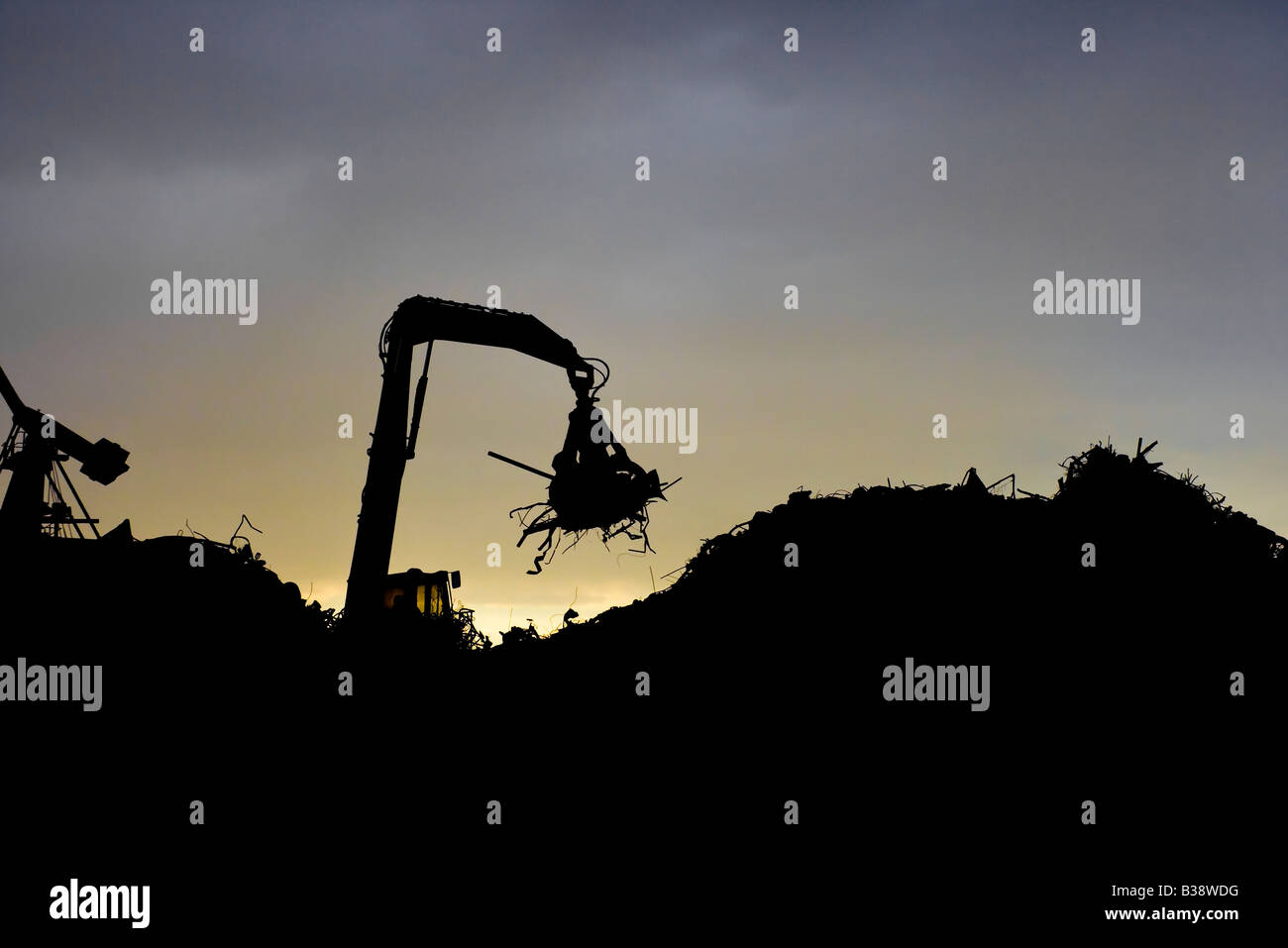 Crane grab operating between piles of scrap metal outlined against an ...