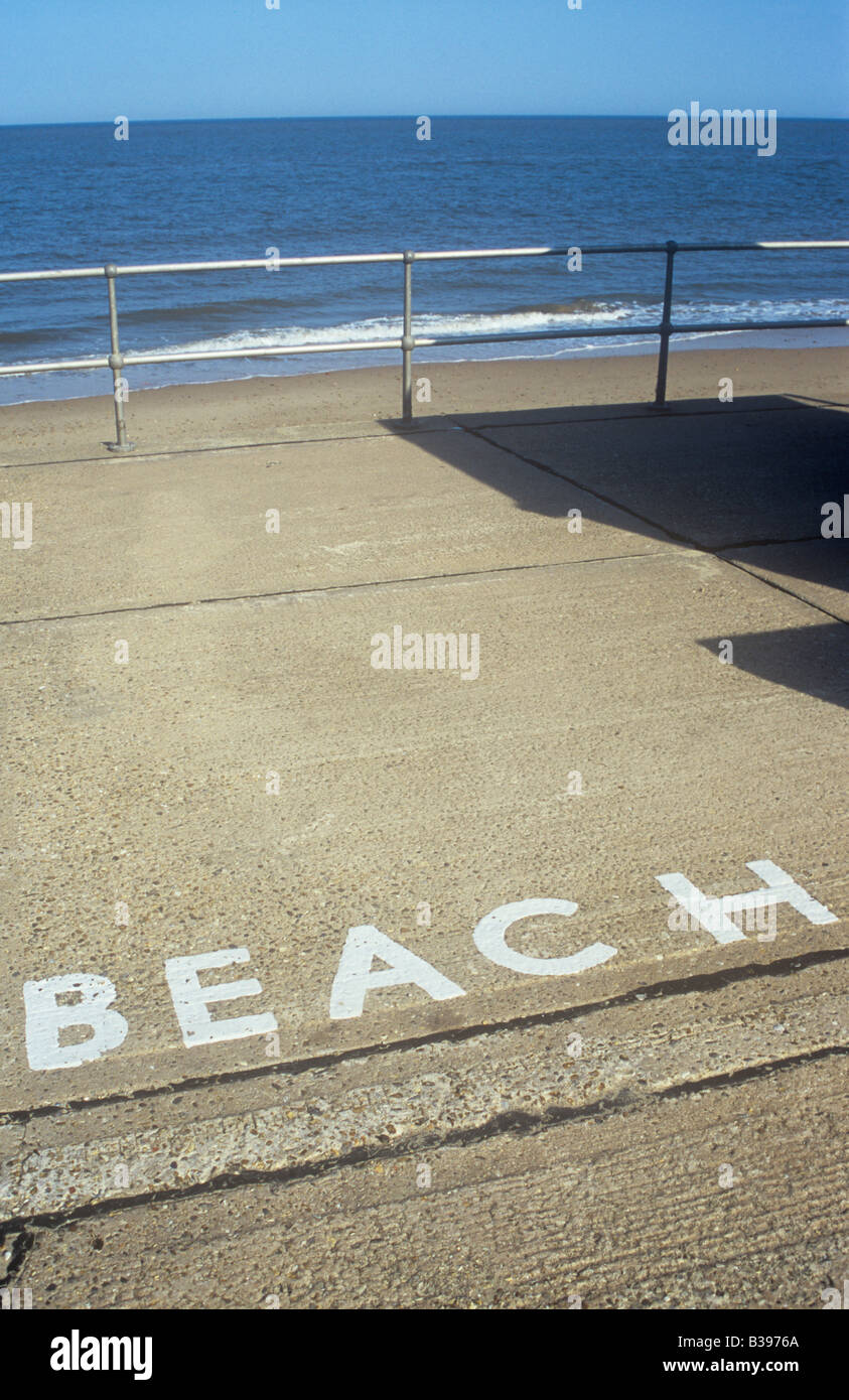 Concrete promenade with shadow of beach-hut and railings with beach sea ...
