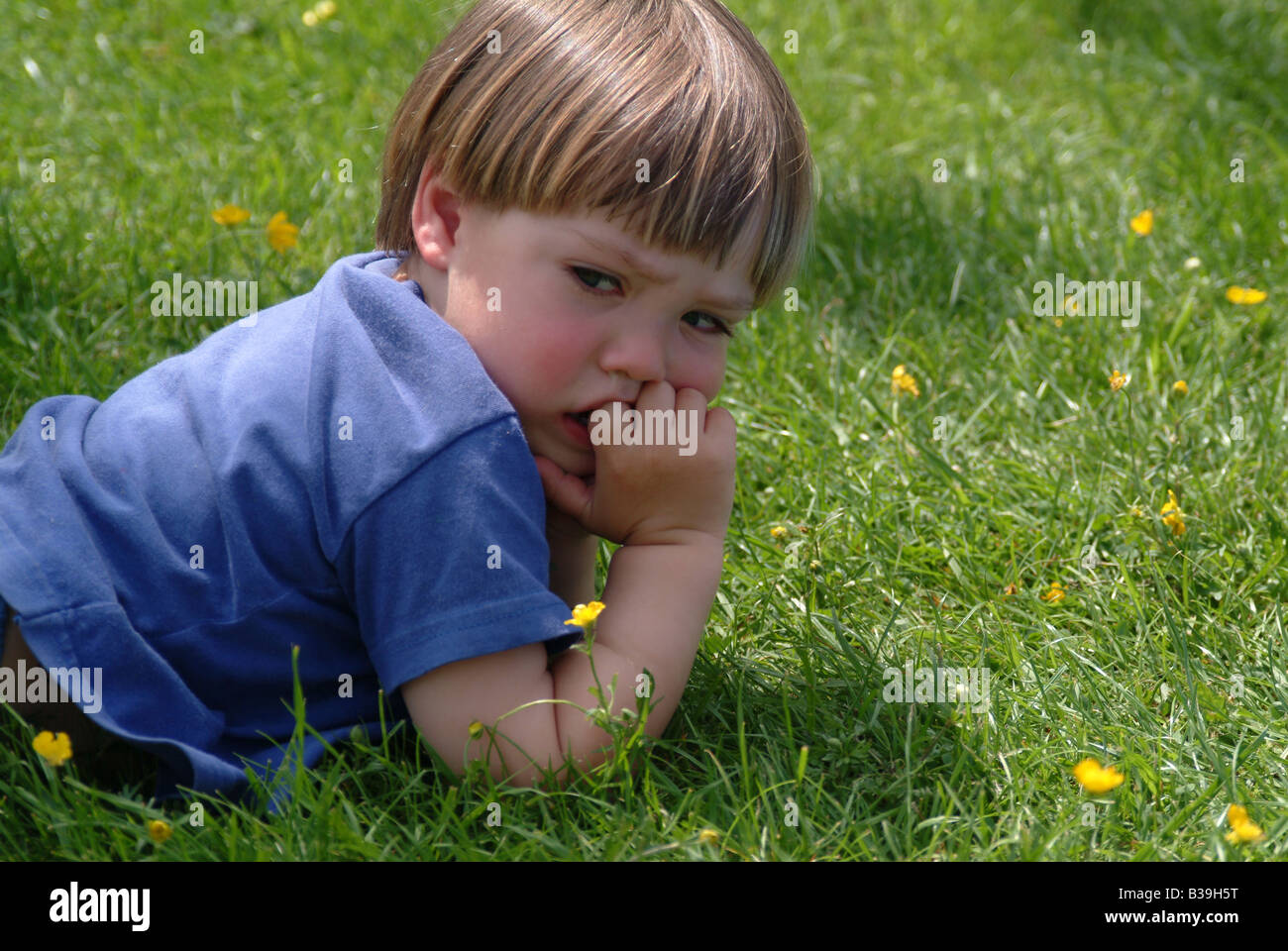 Little boy lying on the grass looking grumpy Stock Photo - Alamy