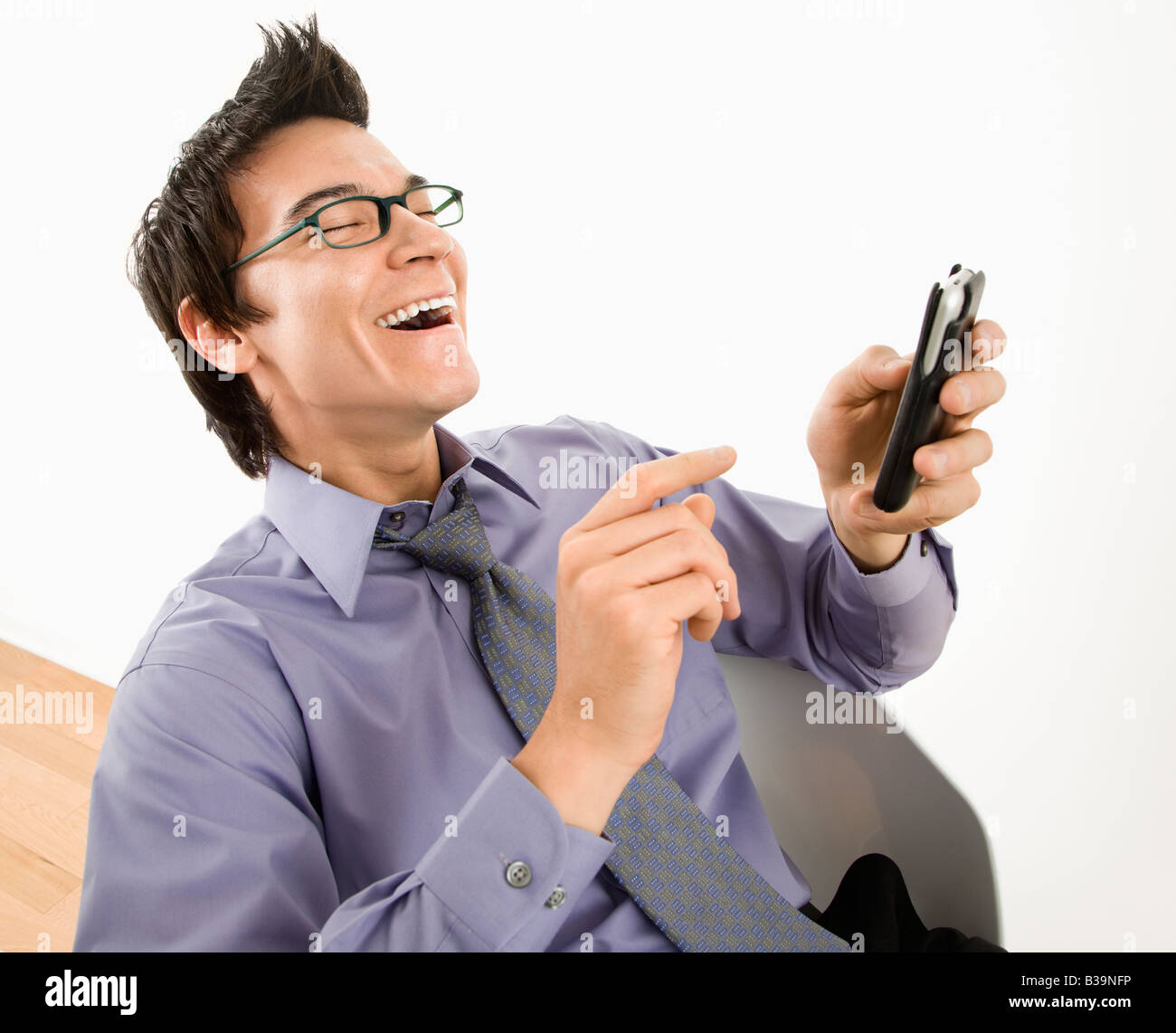 Laughing Asian businessman sitting at desk texting using his pda ...