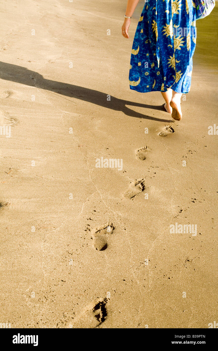 A woman walking on a beach, leaving footprints in the sand on a ...
