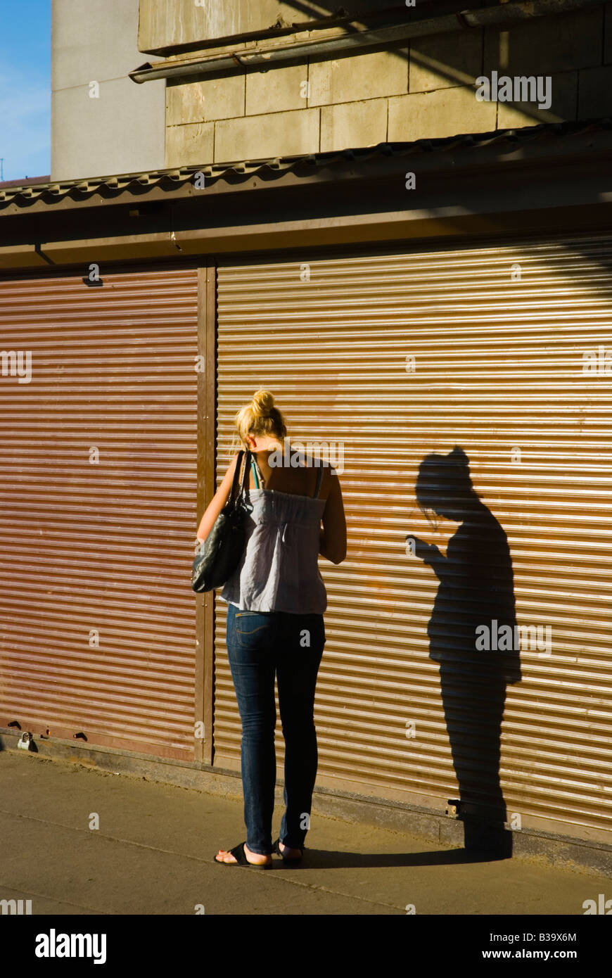 Young woman writing an sms text message in front of shut kiosks in Riga ...