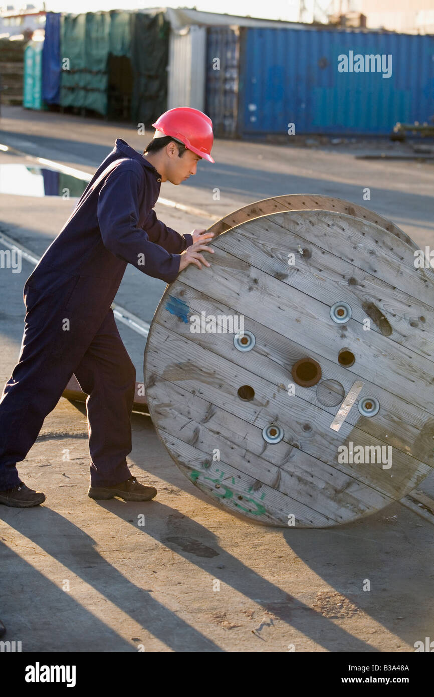 Asian male manual worker pushing wooden spool Stock Photo - Alamy