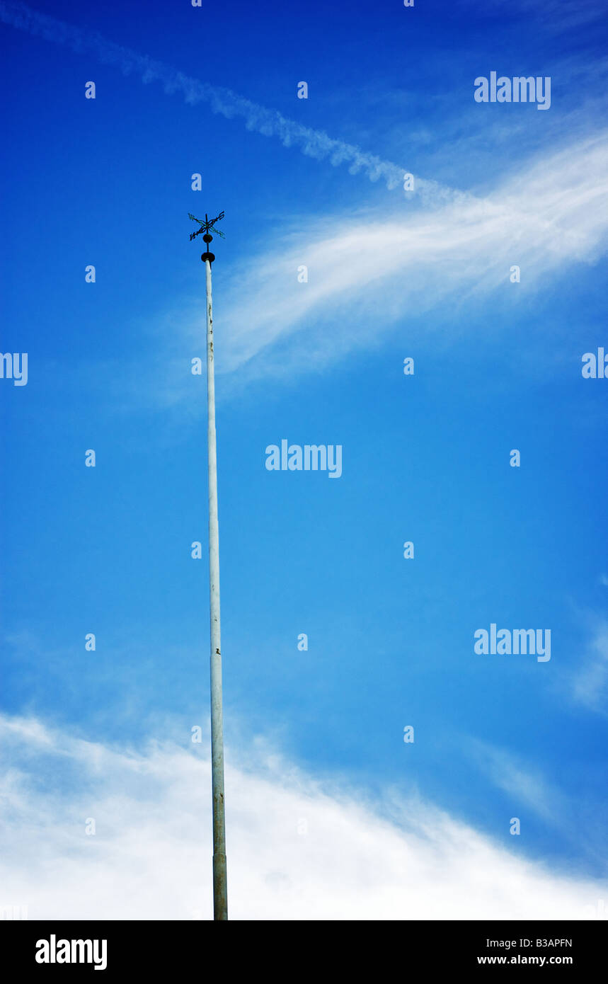 Compass on a tall rusty pole against a blue sky with clouds and jet ...