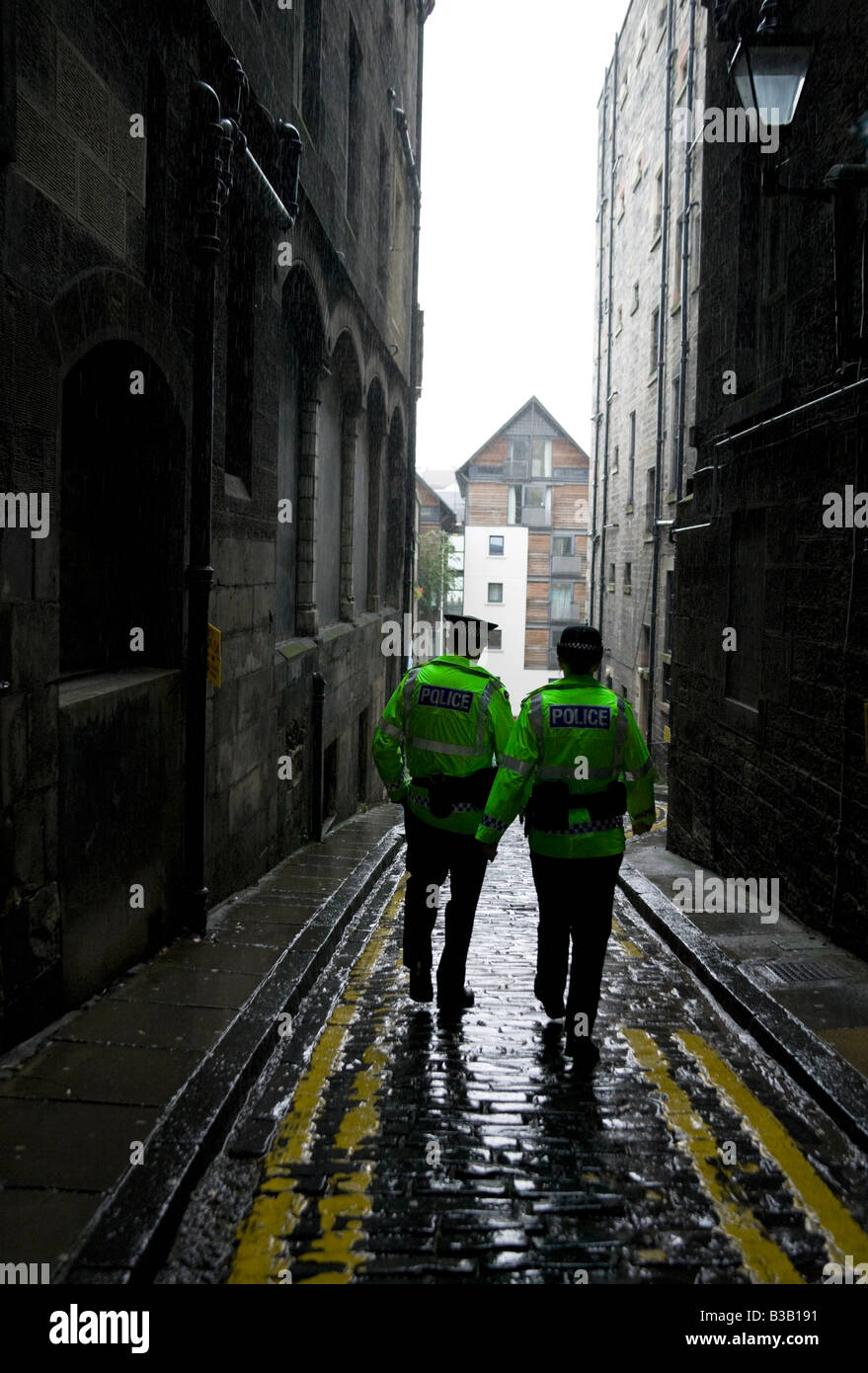 Male and female Police officers walking down a close in pouring rain ...
