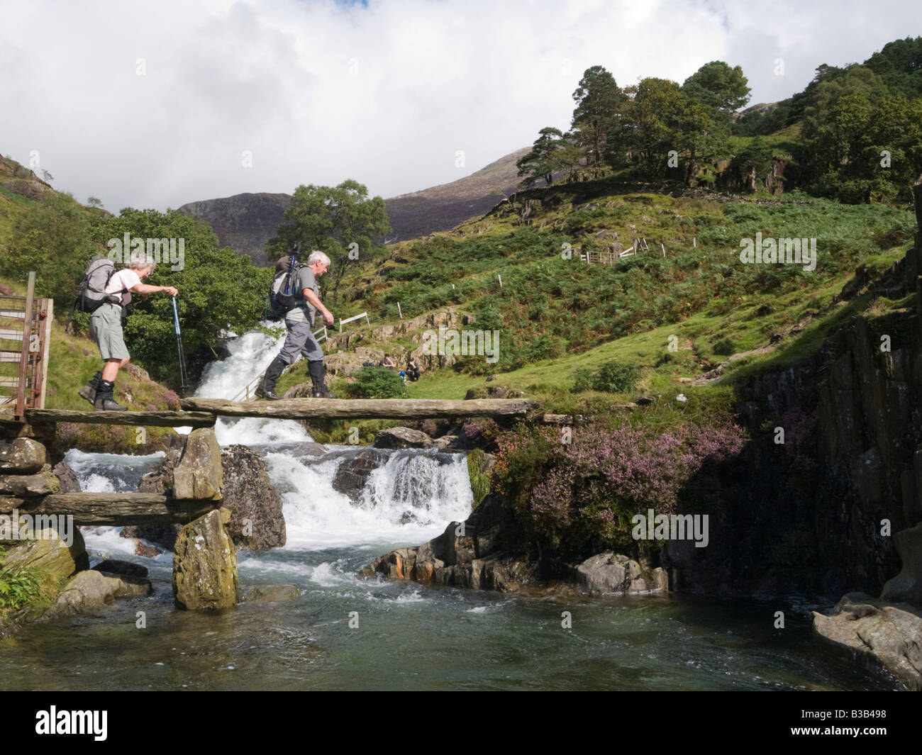 Two walkers crossing footbridge over Afon Cwm Llan river waterfall in ...