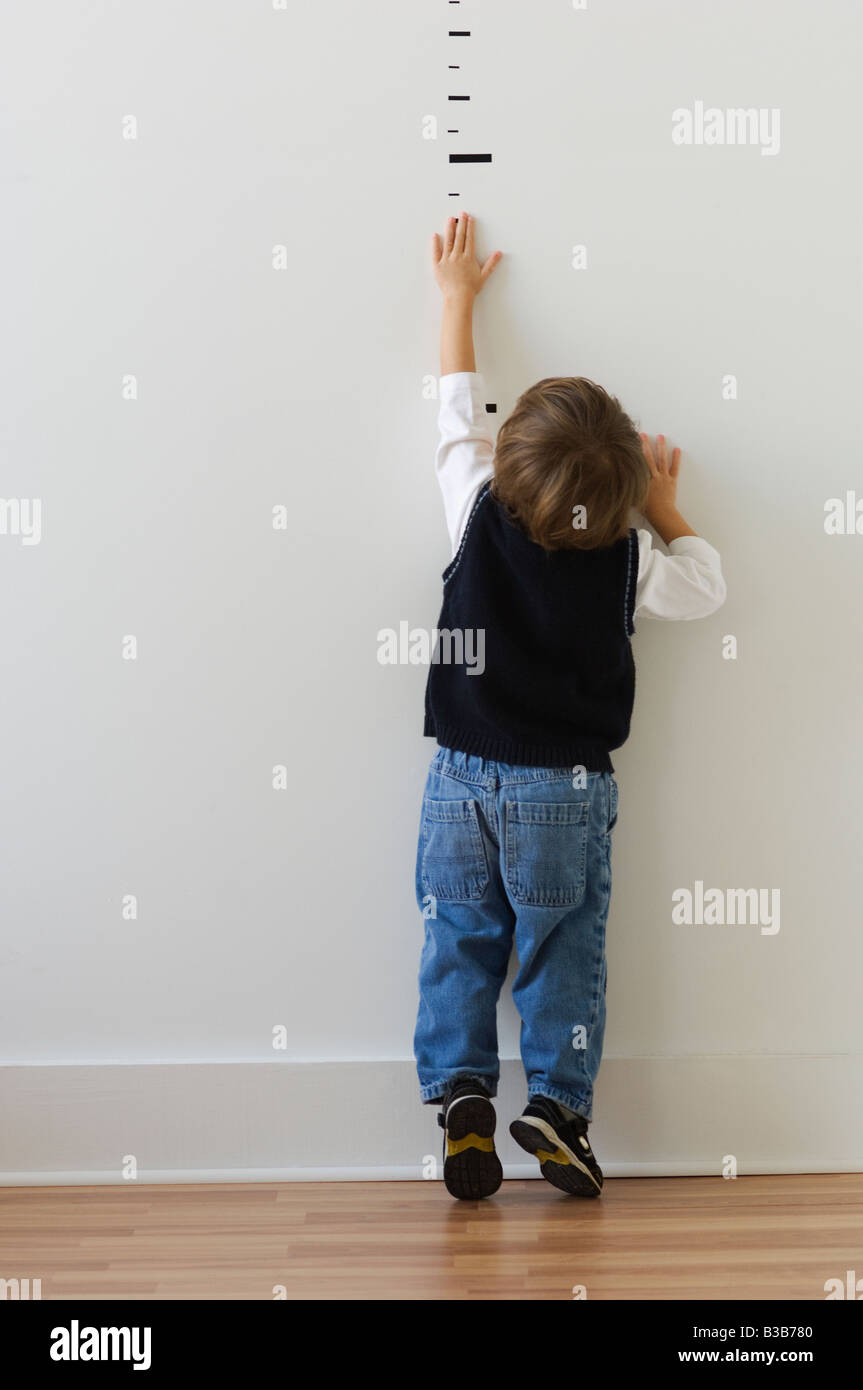 Boy reaching for height markers on wall Stock Photo - Alamy