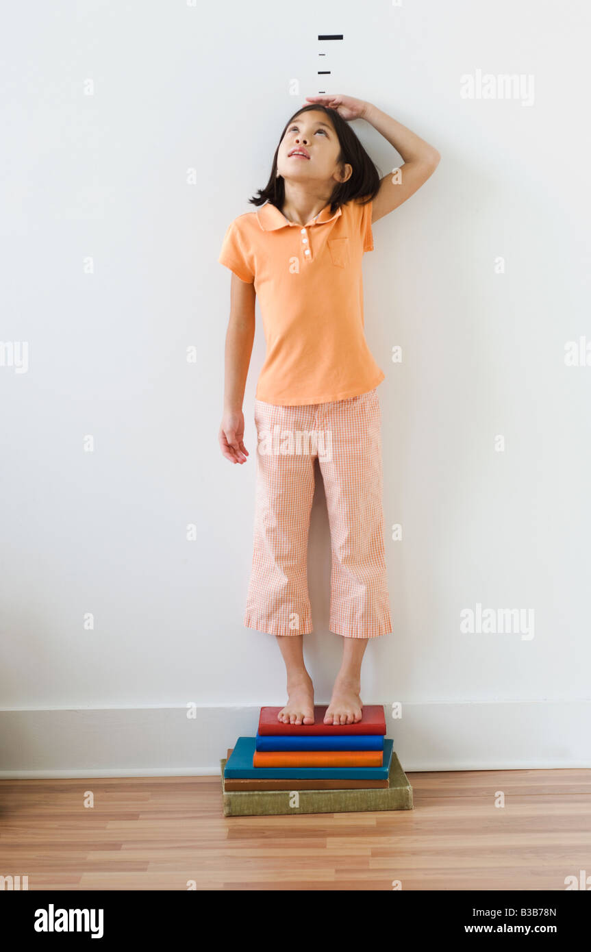 Asian girl standing on books in front of height markers Stock Photo - Alamy