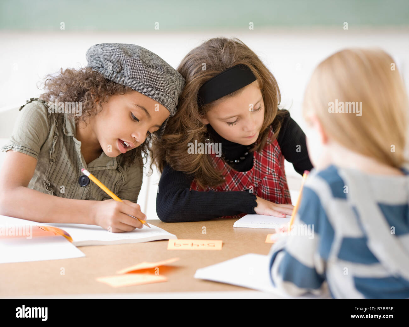 Multi-ethnic girls writing at table Stock Photo - Alamy