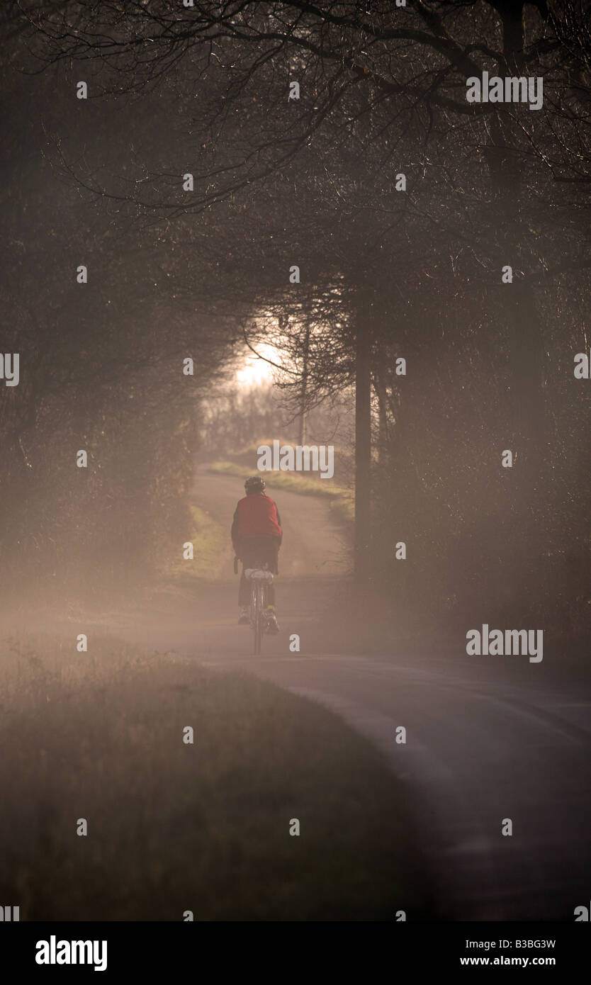 A solitary cyclist makes her down a misty country lane at sunrise in ...