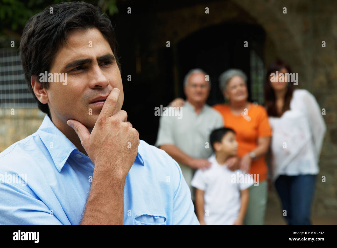 Hispanic man thinking with family in background Stock Photo - Alamy