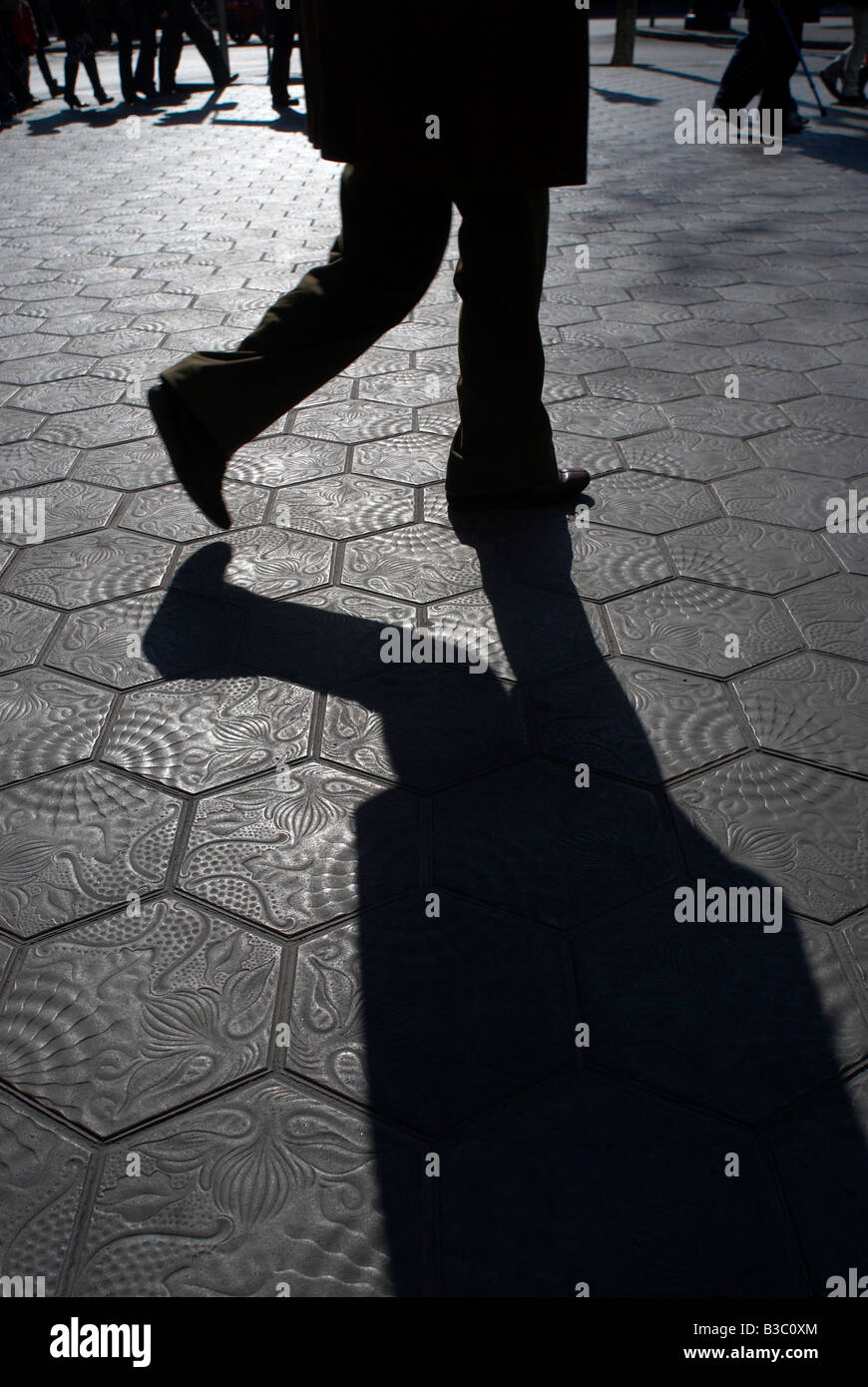 Man's legs and shadow walking on tiled streets Stock Photo - Alamy
