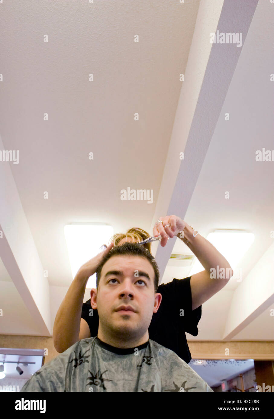 A young man getting his hair cut by a hairdresser at the beauty salon ...