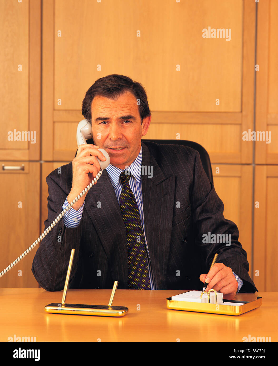 Businessman talking over phone while sitting in office Stock Photo - Alamy
