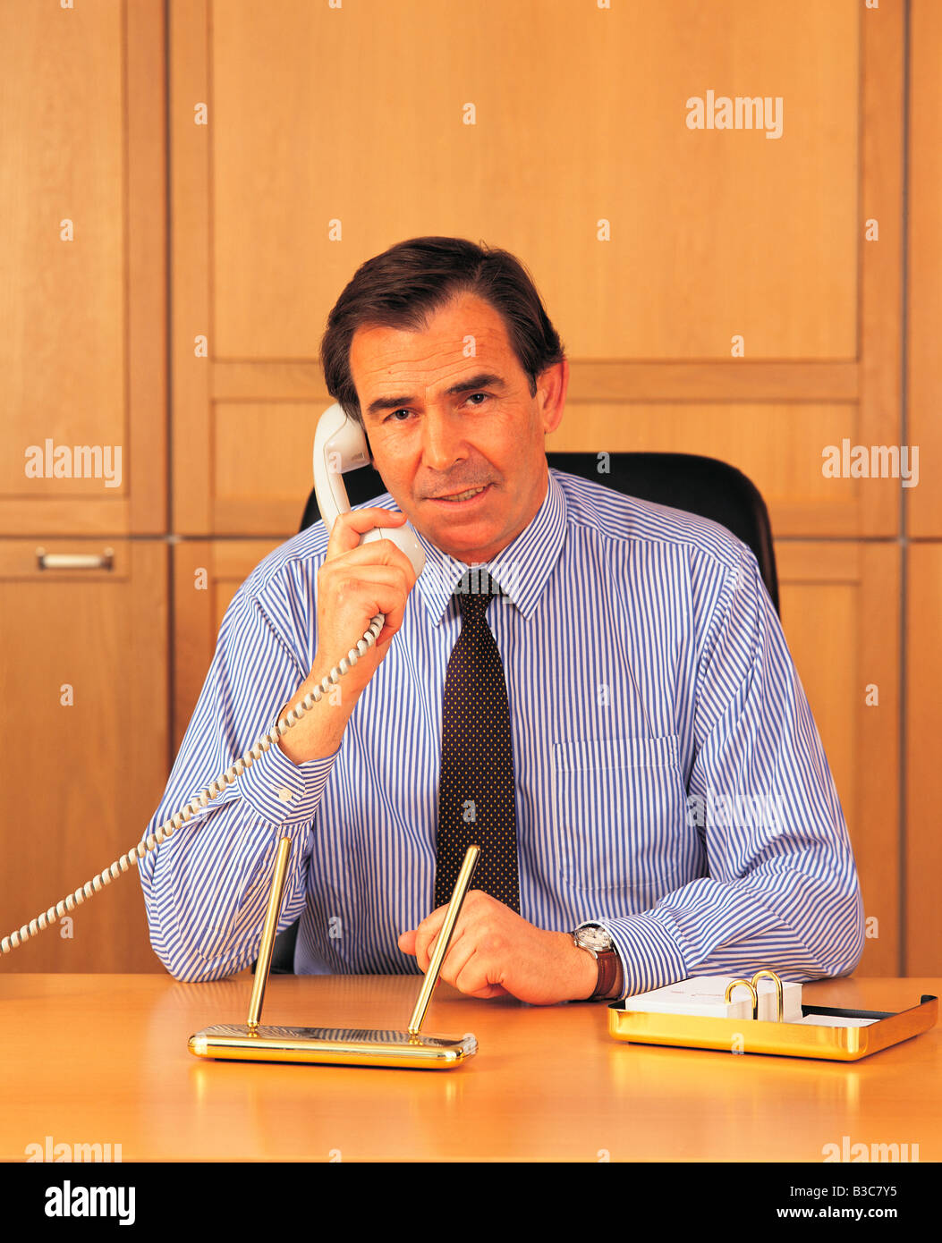 Businessman talking over phone while sitting in office Stock Photo - Alamy