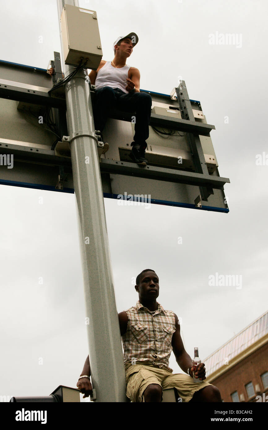 Two Men Sitting On Pole Traffic Sign Mast Having Better View On Street